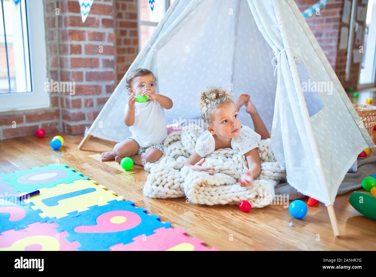 Beautiful toddlers playing inside tipi over blanket around lots of toys ...
