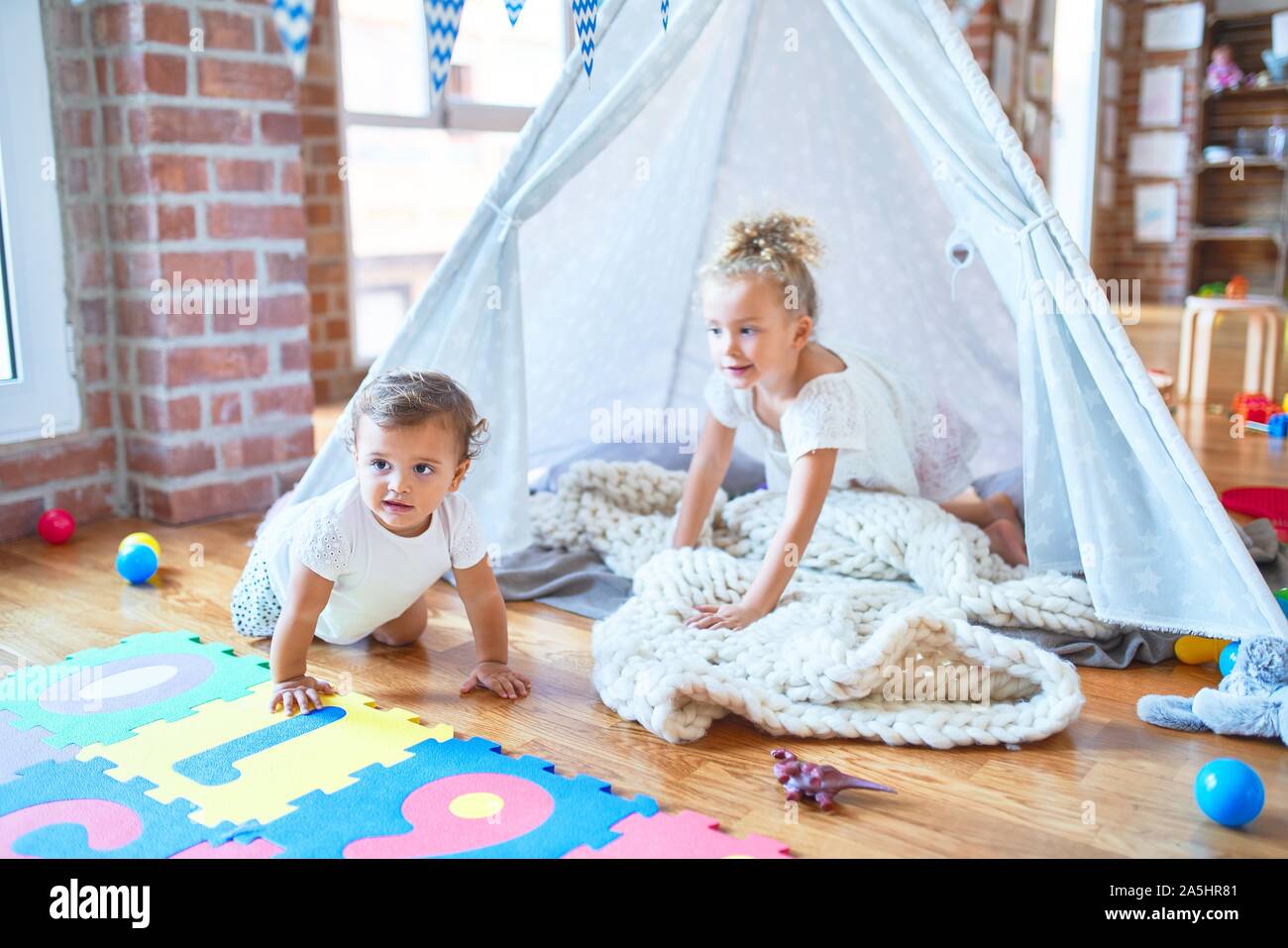 Beautiful toddlers playing inside tipi over blanket around lots of toys ...