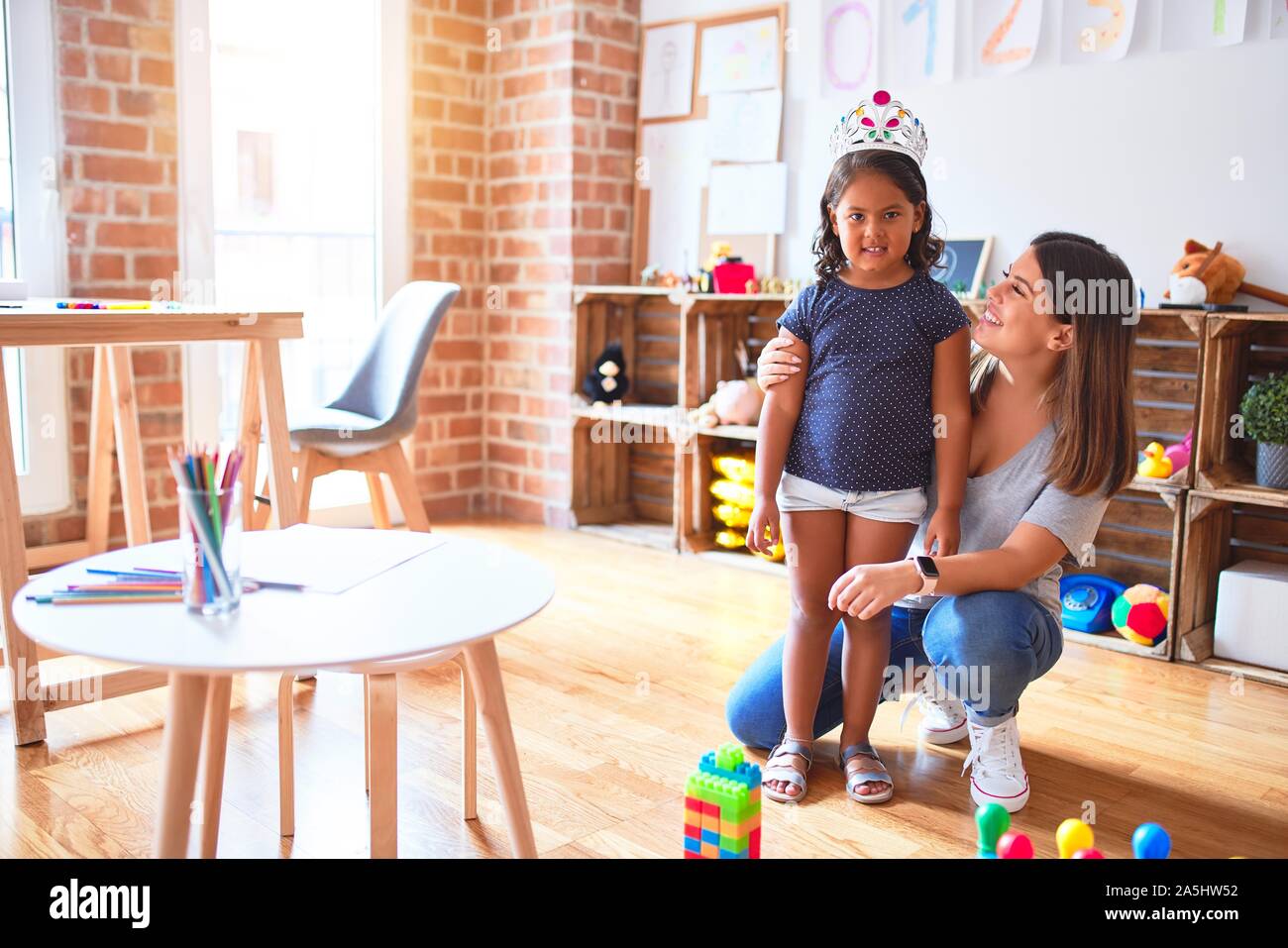 Beautiful teacher looking at toddler girl wearing princess crown at ...