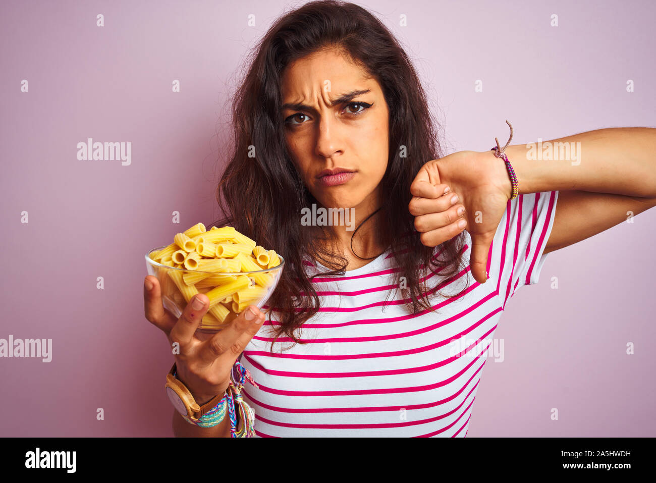 Young beautiful woman holding bowl with dry macaroni pasta over ...