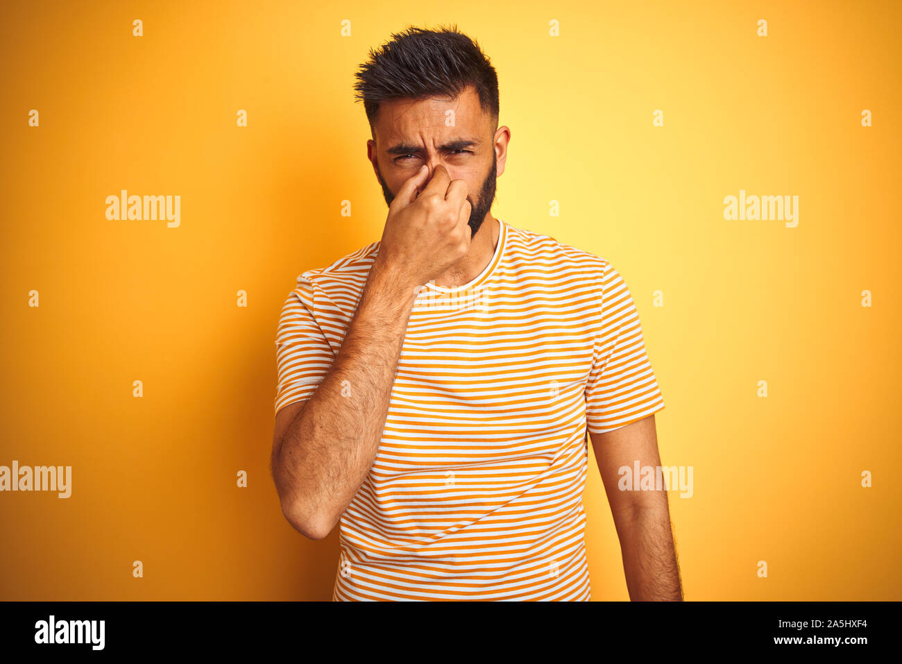 Young indian man wearing t-shirt standing over isolated yellow ...