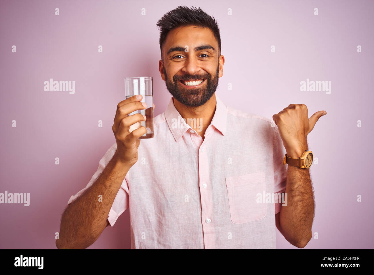 Young handsome indian man dinking glass of water over isolated pink ...