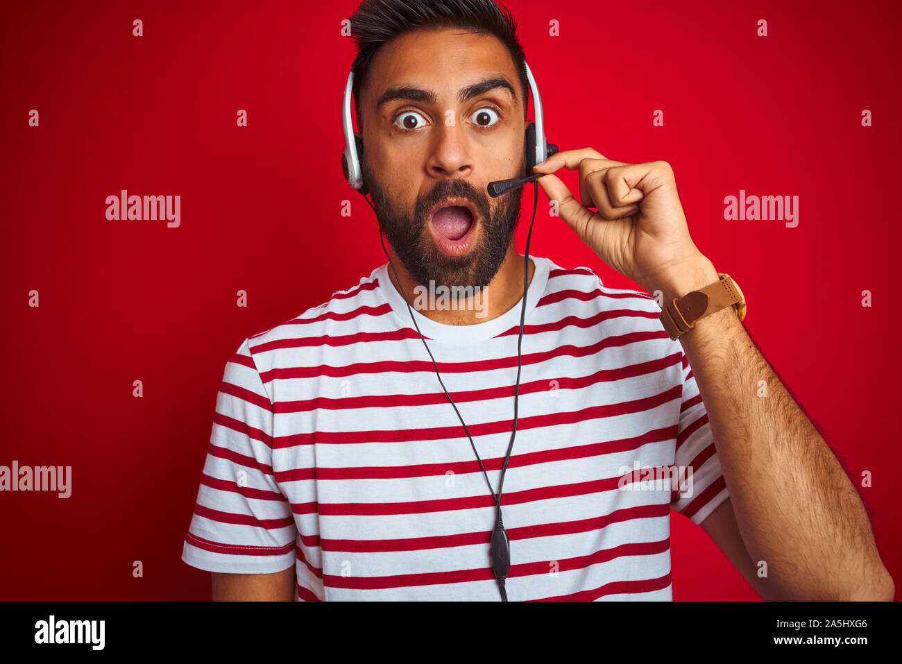 Young indian call center agent man using headset over isolated red ...