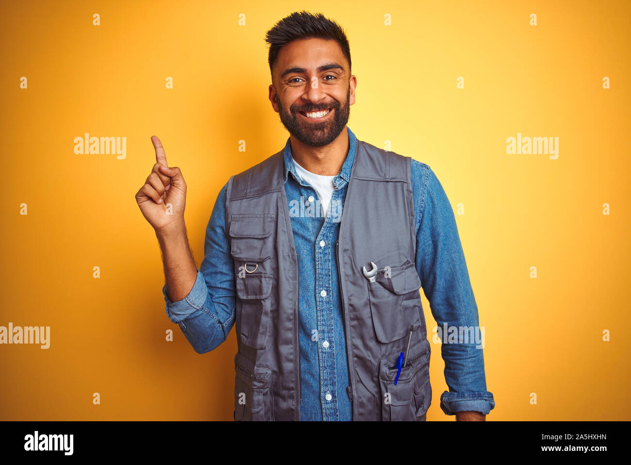 Handsome indian technician man wearing uniform over isolated yellow ...