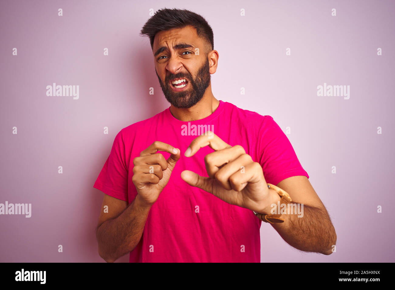 Young indian man wearing t-shirt standing over isolated pink background ...