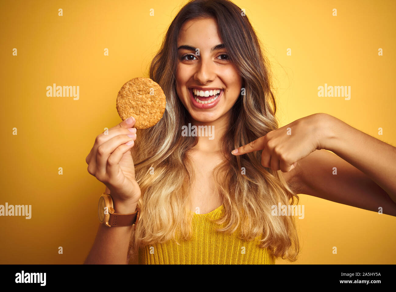Young beautiful woman eating biscuit over grey isolated background with ...