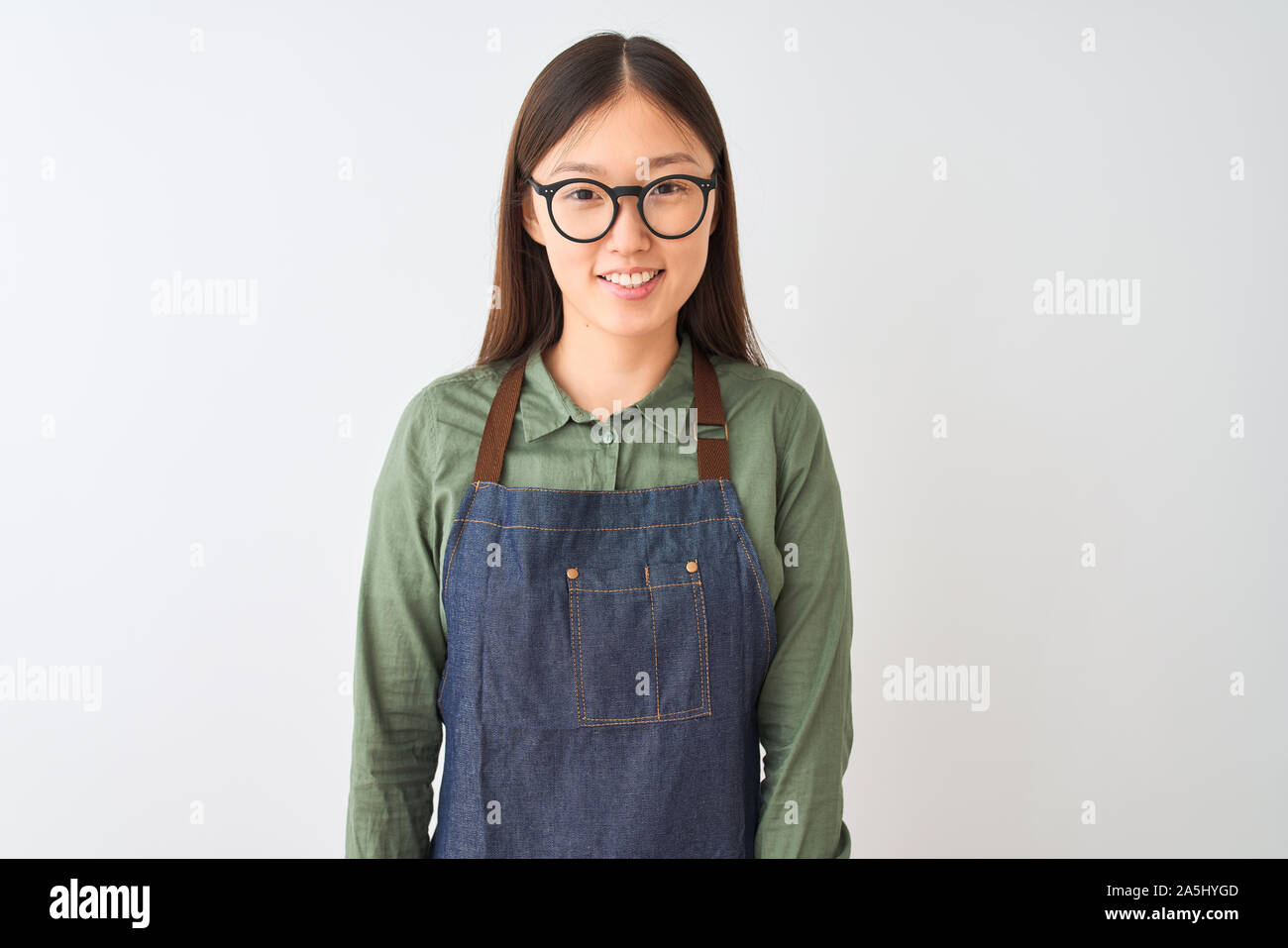 Young chinese shopkeeper woman wearing apron and glasses over isolated ...
