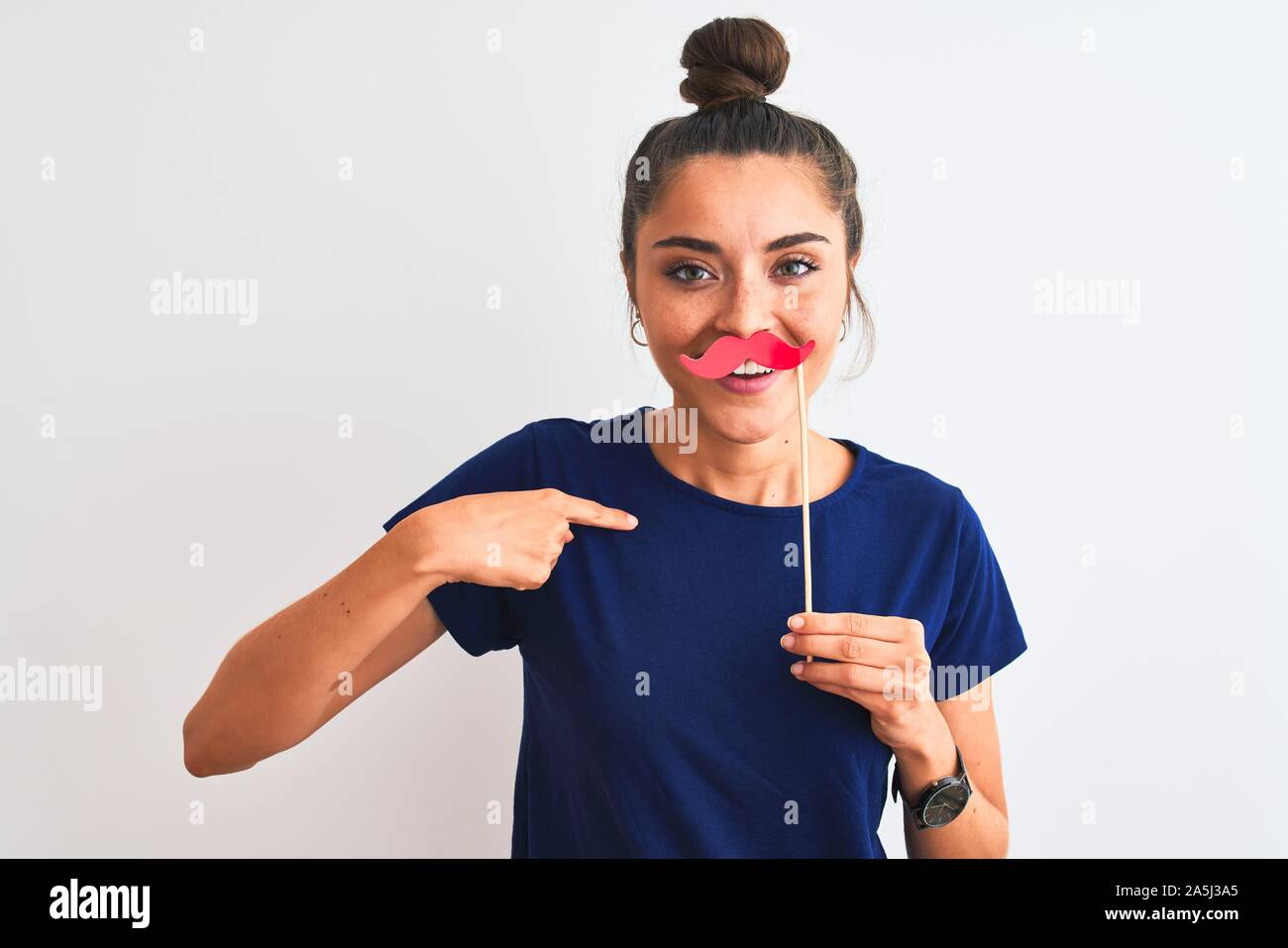 Young beautiful woman holding fanny party mustache over isolated white ...