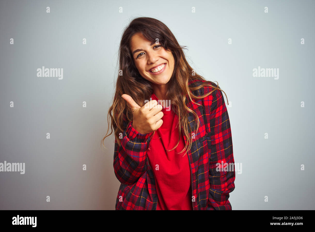 Young beautiful woman wearing red t-shirt and jacket standing over ...