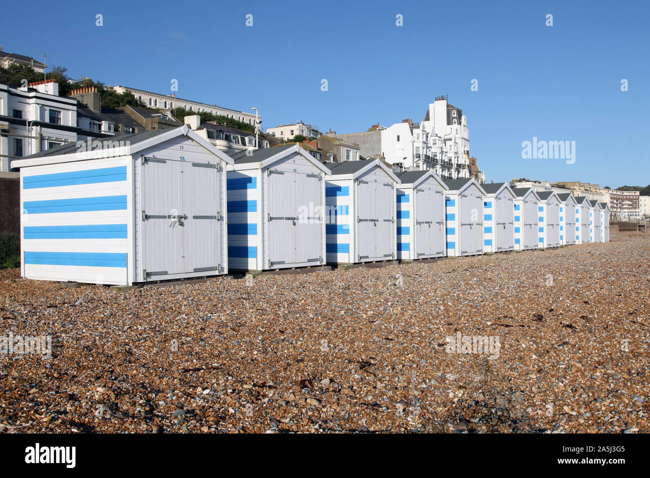A row of blue and white striped beach huts on a stony Hastings beach ...