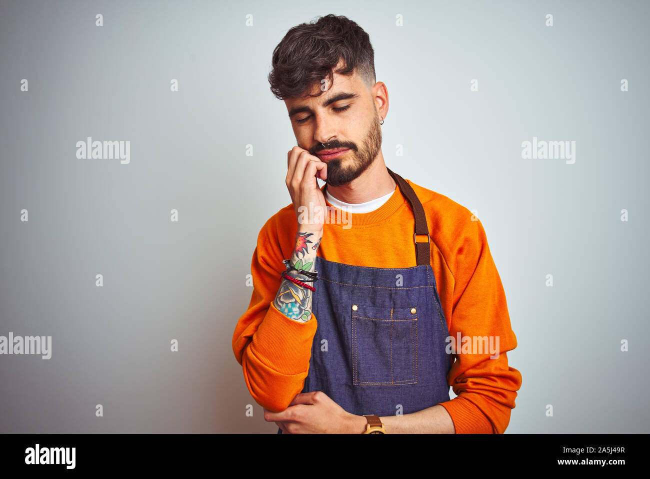 Young shopkeeper man with tattoo wearing apron standing over isolated ...