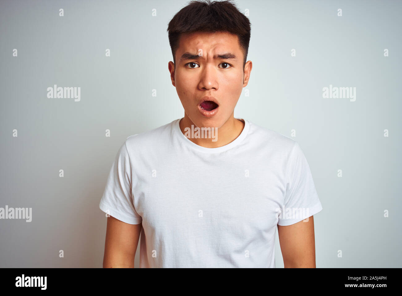 Young asian chinese man wearing t-shirt standing over isolated white ...