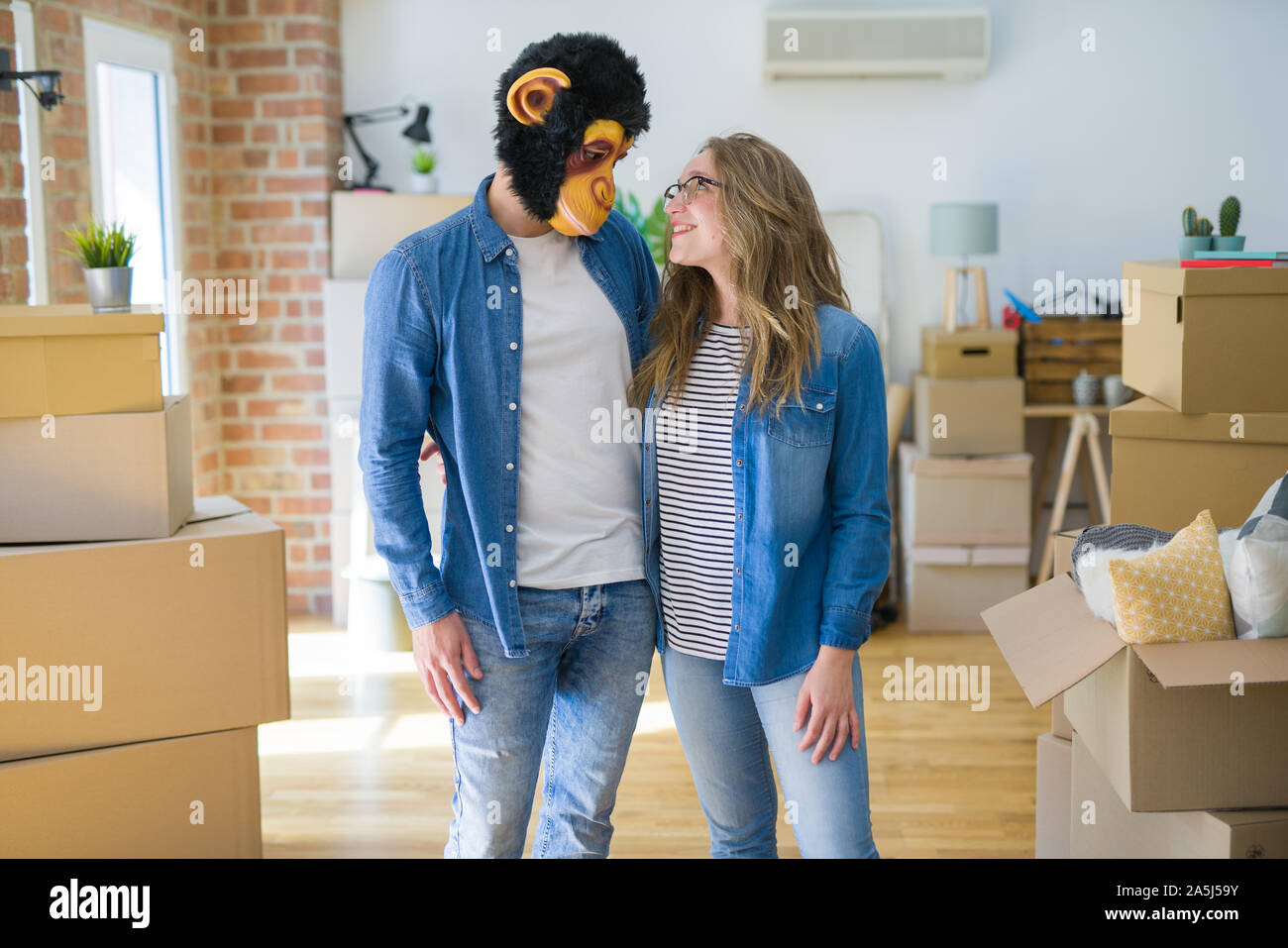 Young couple having fun wearing a monkey mask moving to a new apartment ...