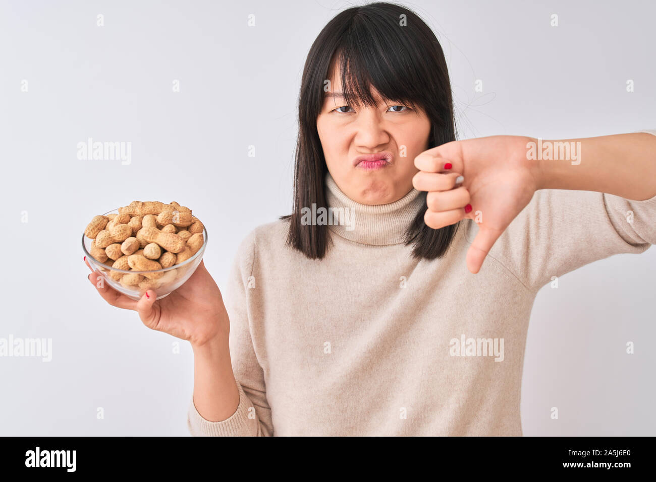 Young beautiful Chinese woman holding bowl with peanuts over isolated ...