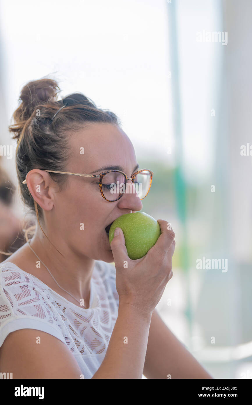 Face of woman eating juicy apple while looking down wearing glasses and ...