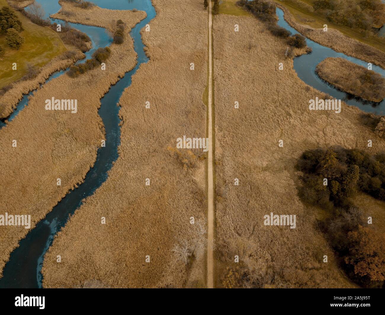 Aerial shot of a pathway in the middle of a dry grassy field with trees ...