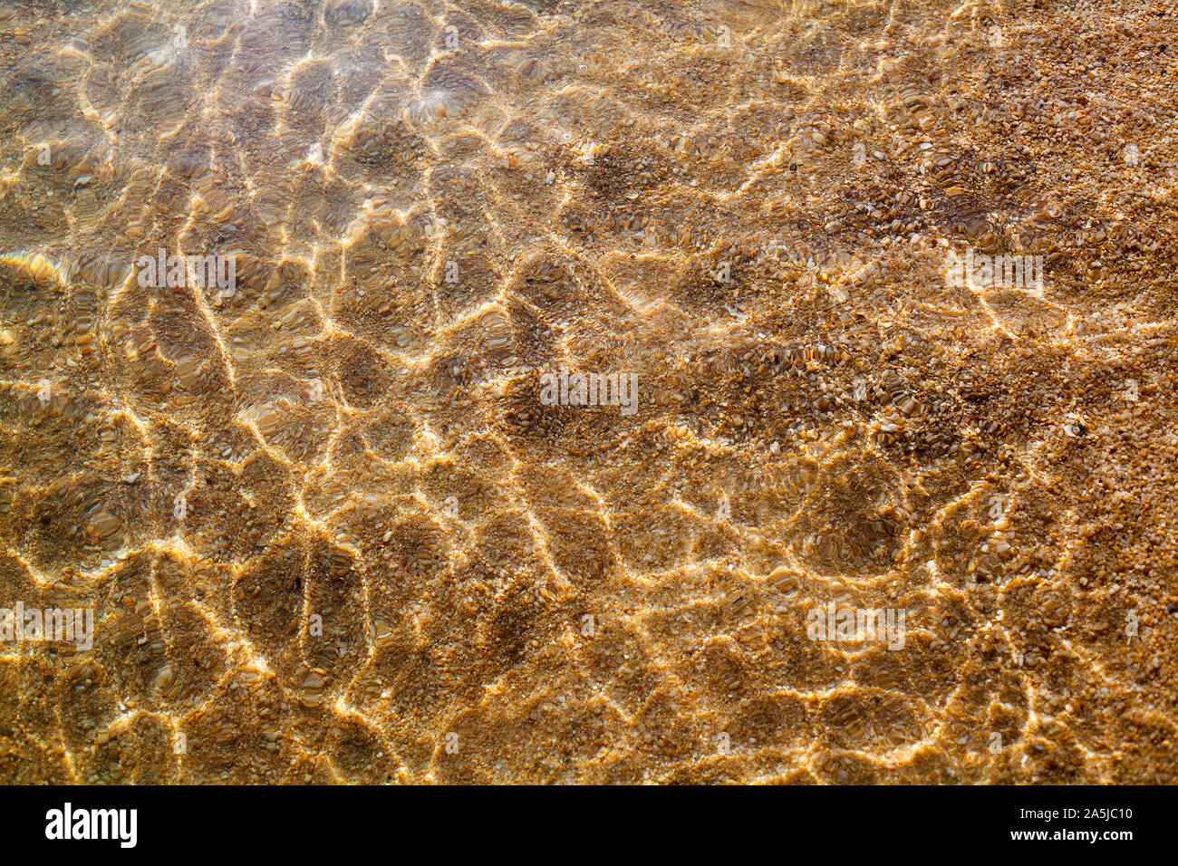 Golden sand under clear sea water and sunlight glow reflection close up ...