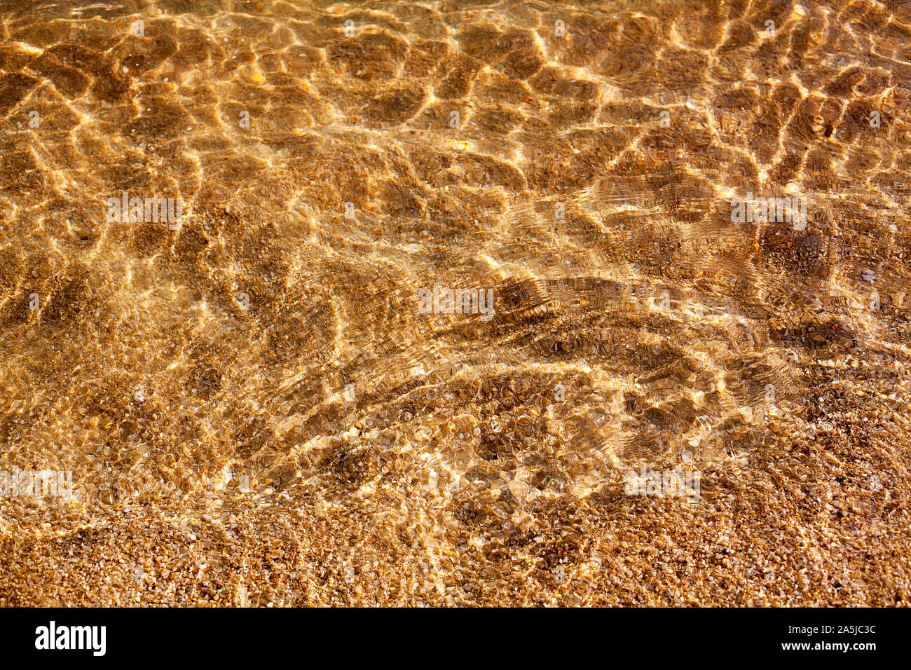 Golden sand under clear sea water and sunlight glow reflection close up ...