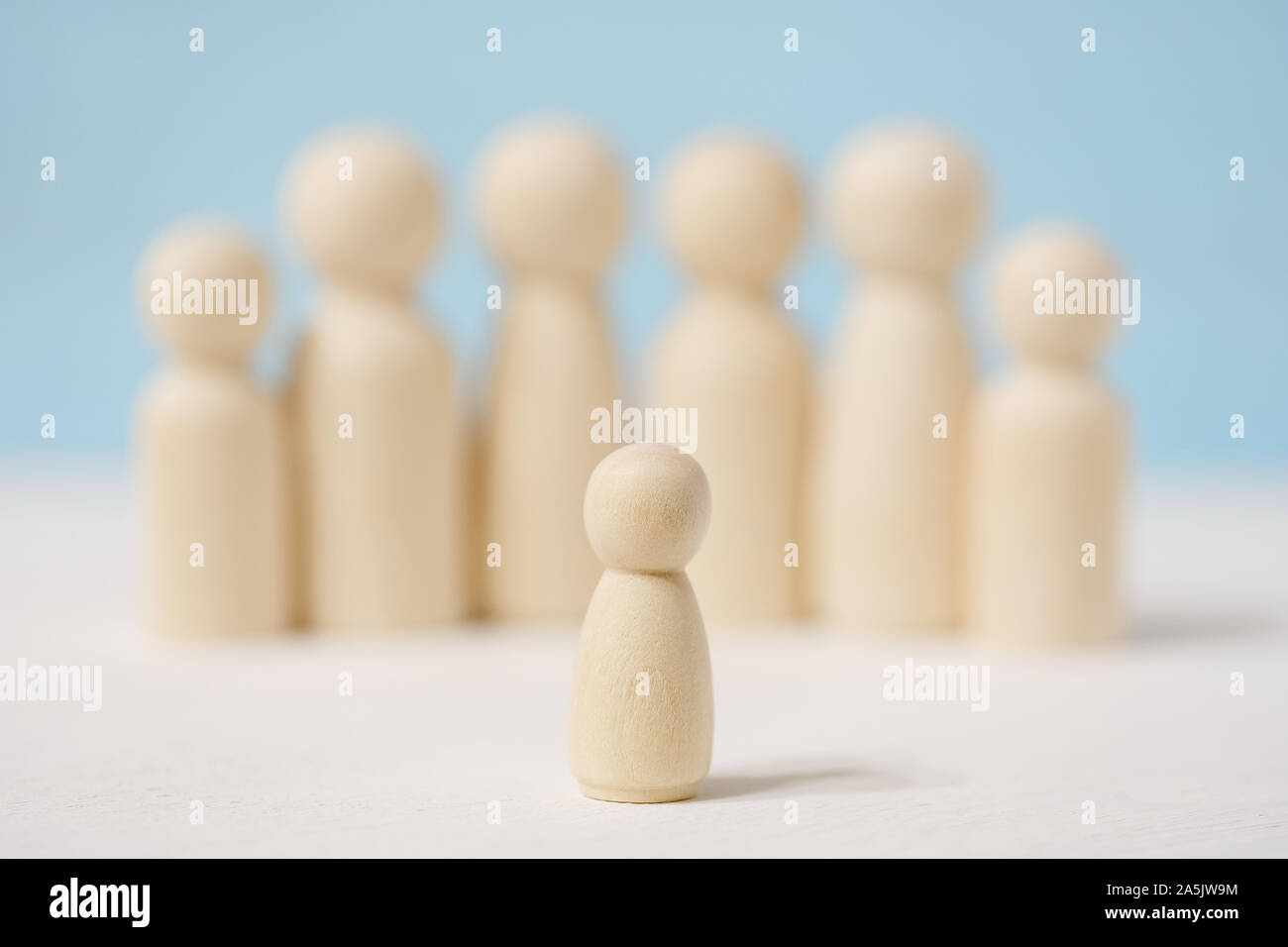 Abstract wooden faceless figures of man and people behind him on blue ...