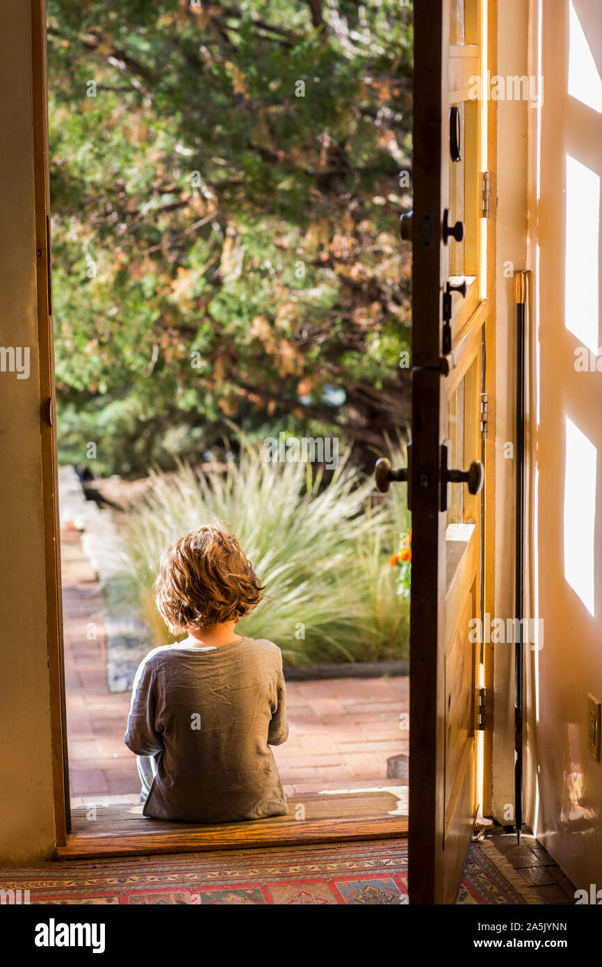 rear view of 5 year old boy sitting on his doorstep in early morning ...