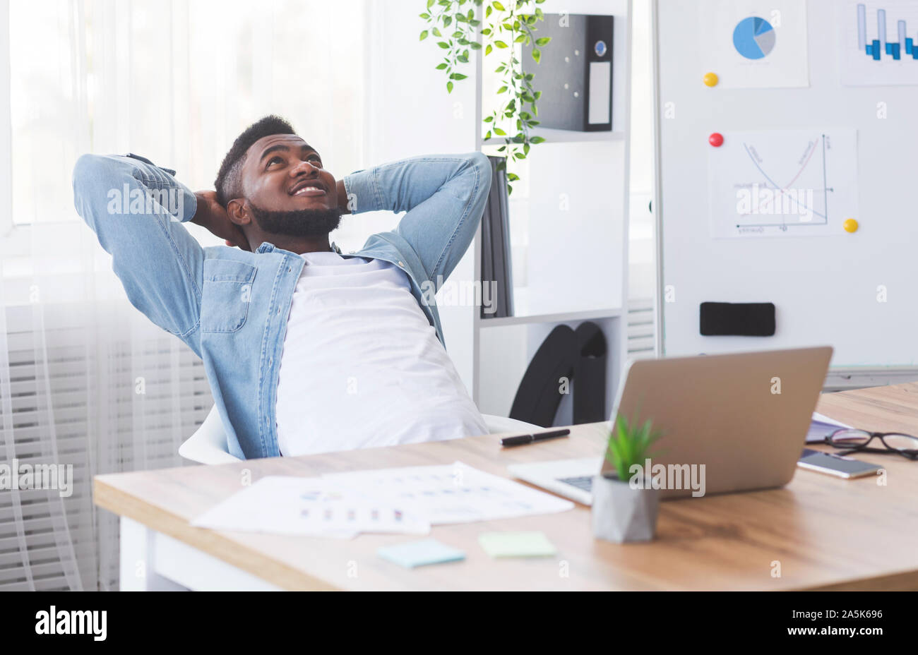 Dreamy black employee resting at workplace with hands behind head Stock ...