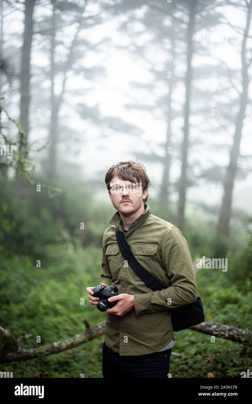 Portrait of photographer standing outdoors in forest holding camera ...