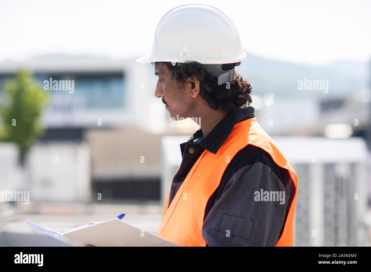 Male engineer outside industrial building writing in notebook, side ...