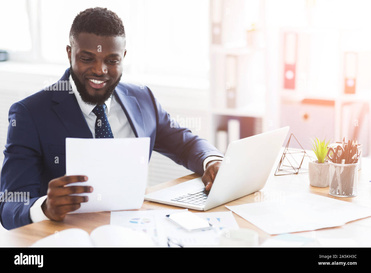 Satisfied black businessman checking documents, sitting in modern ...