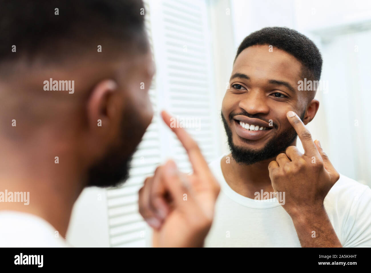 Cheerful black man applying pampering cream on face in bathroom Stock ...