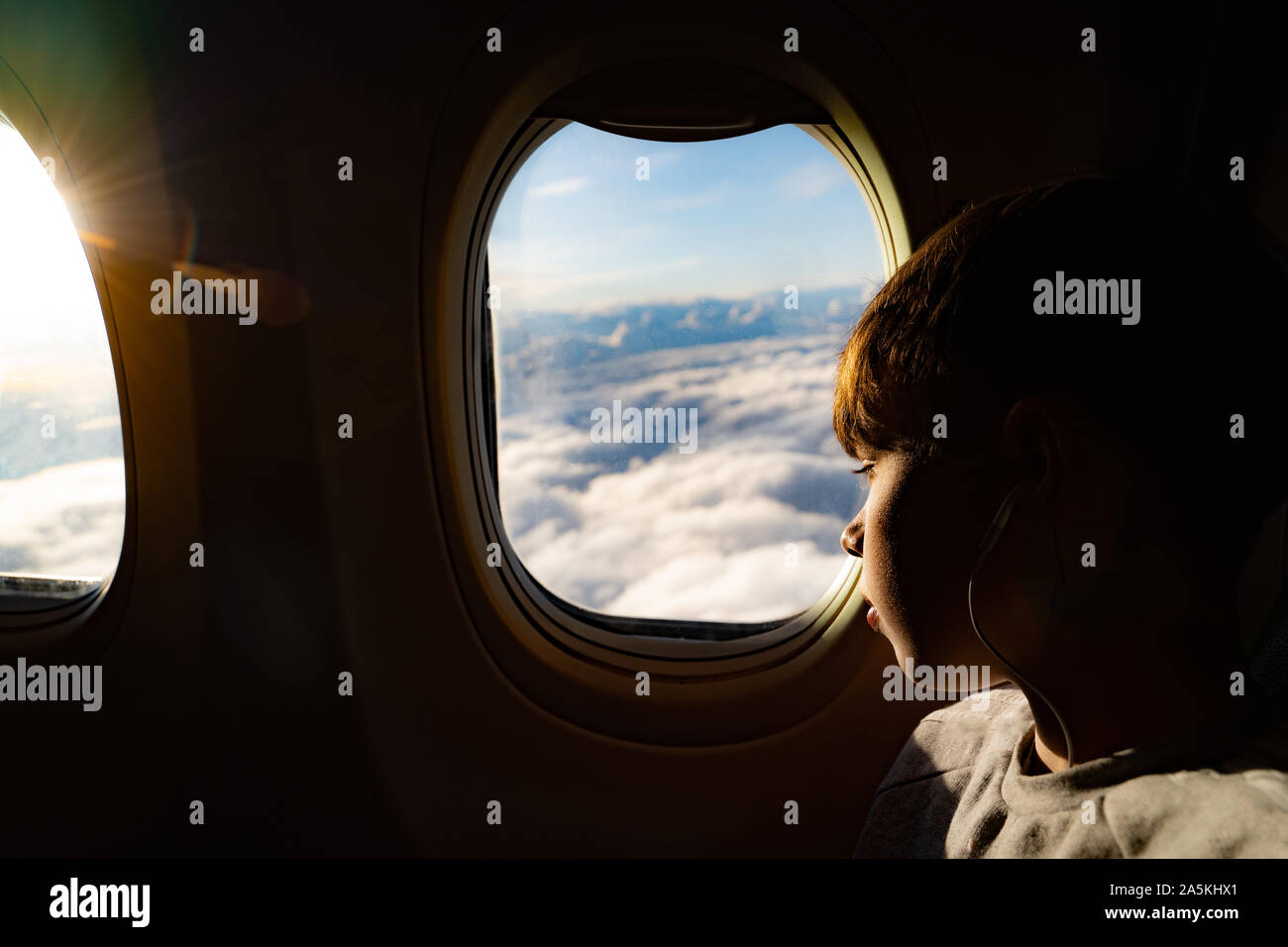 Teenage boy looking out through airplane window at clouds on airplane ...