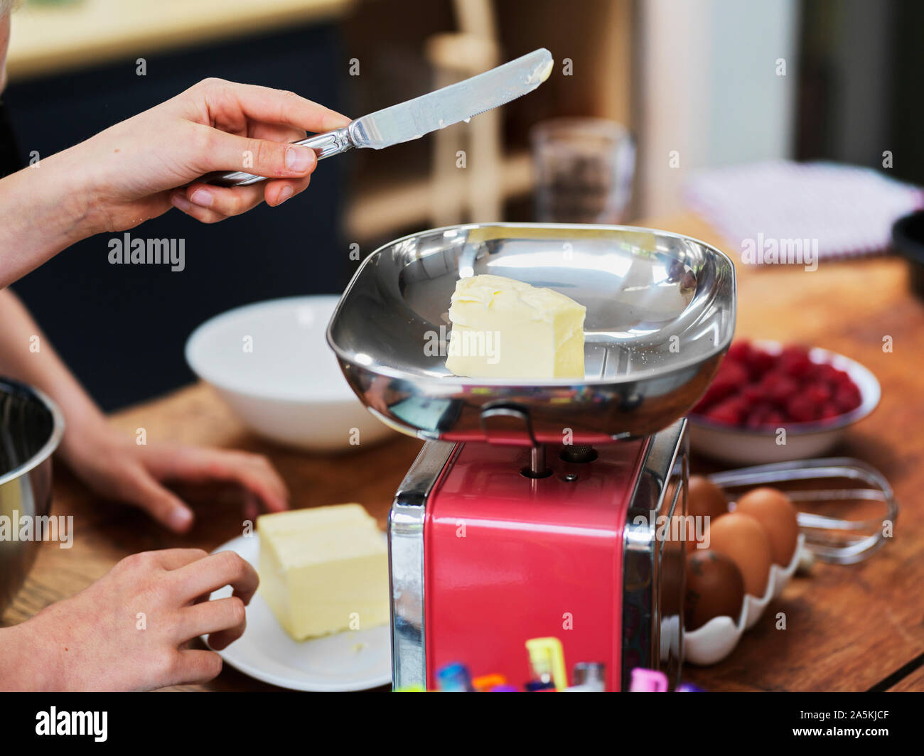 Girl and her sister baking a cake, weighing butter on kitchen scales ...