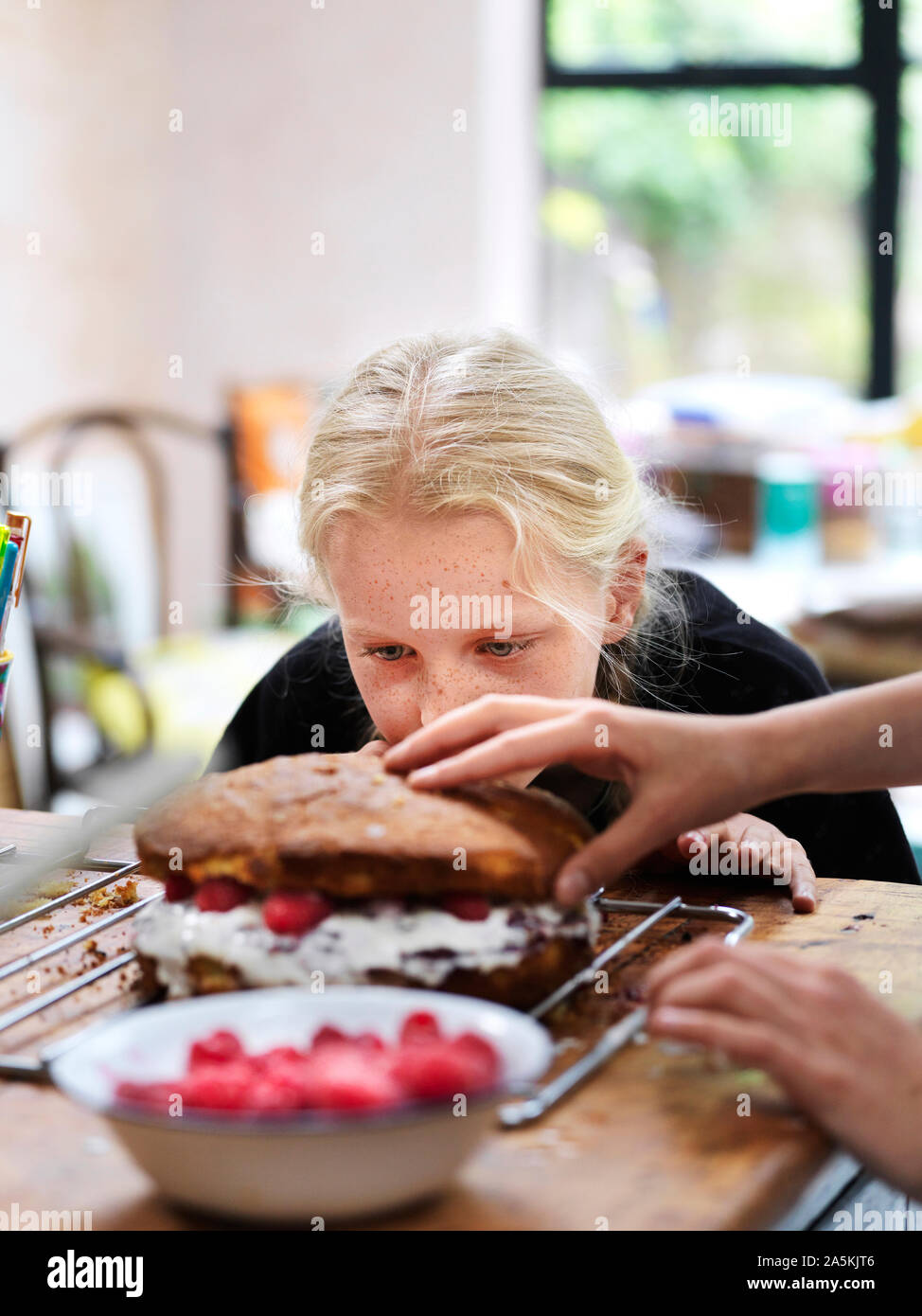 Girl and her sister baking a cake, putting on top layer at kitchen ...