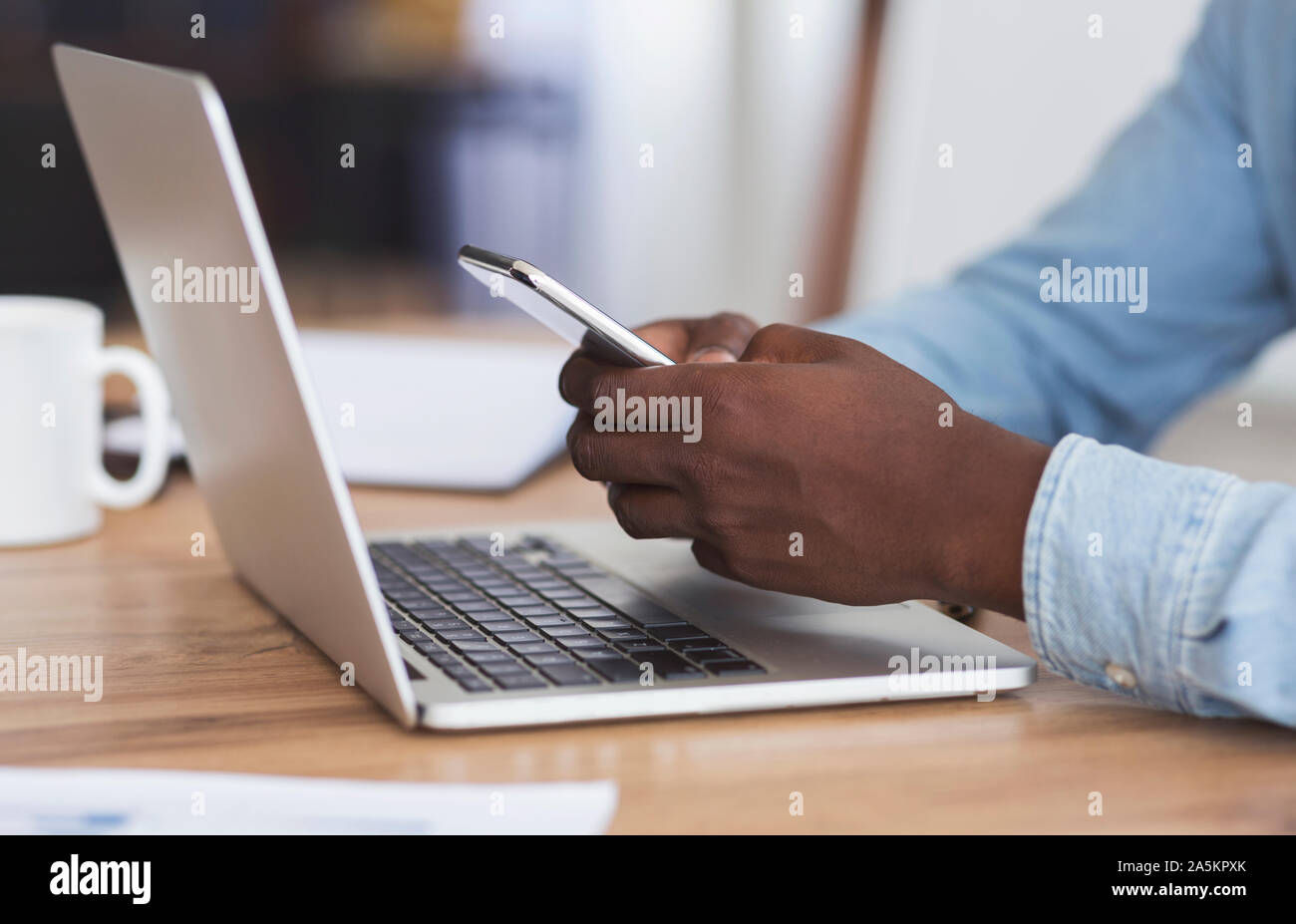 Black man typing message on smartphone and working with laptop Stock ...