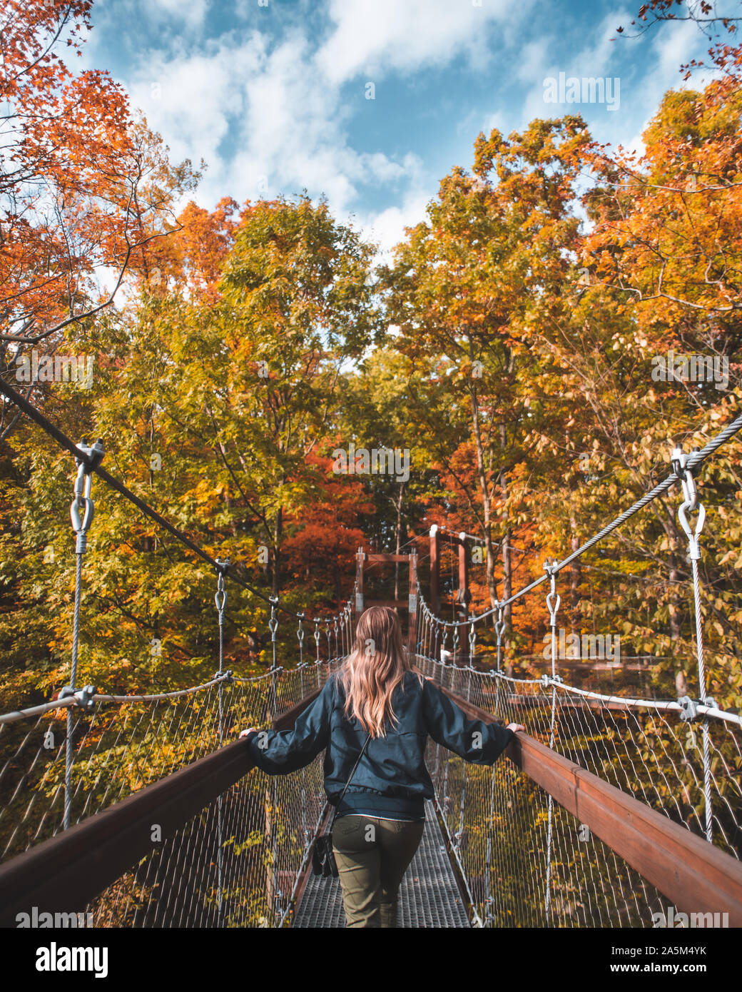 Girl walking across a bridge in the fall trees Stock Photo - Alamy