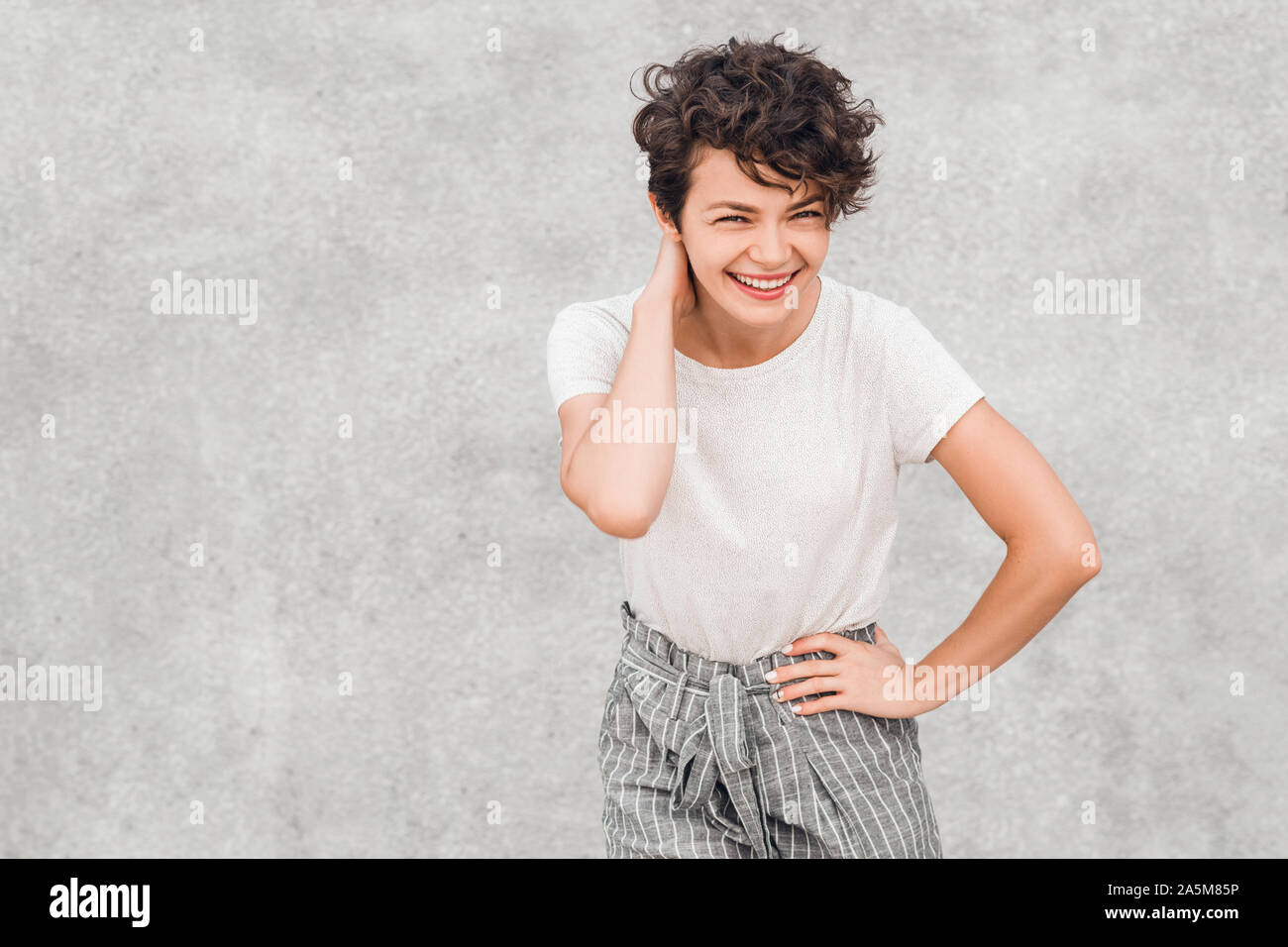 Charming young woman with creative hairstyle is smiling and posing with ...