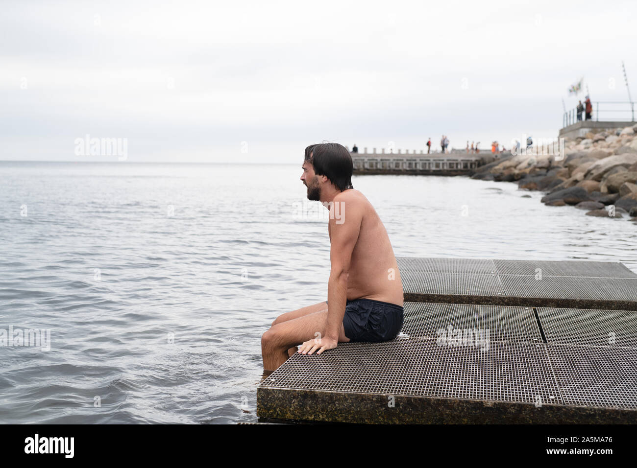 Wet man sitting with feet in the water after jumping in Stock Photo - Alamy