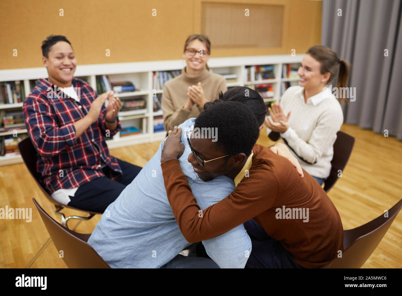 Portrait of two young people hugging in support group meeting, both ...