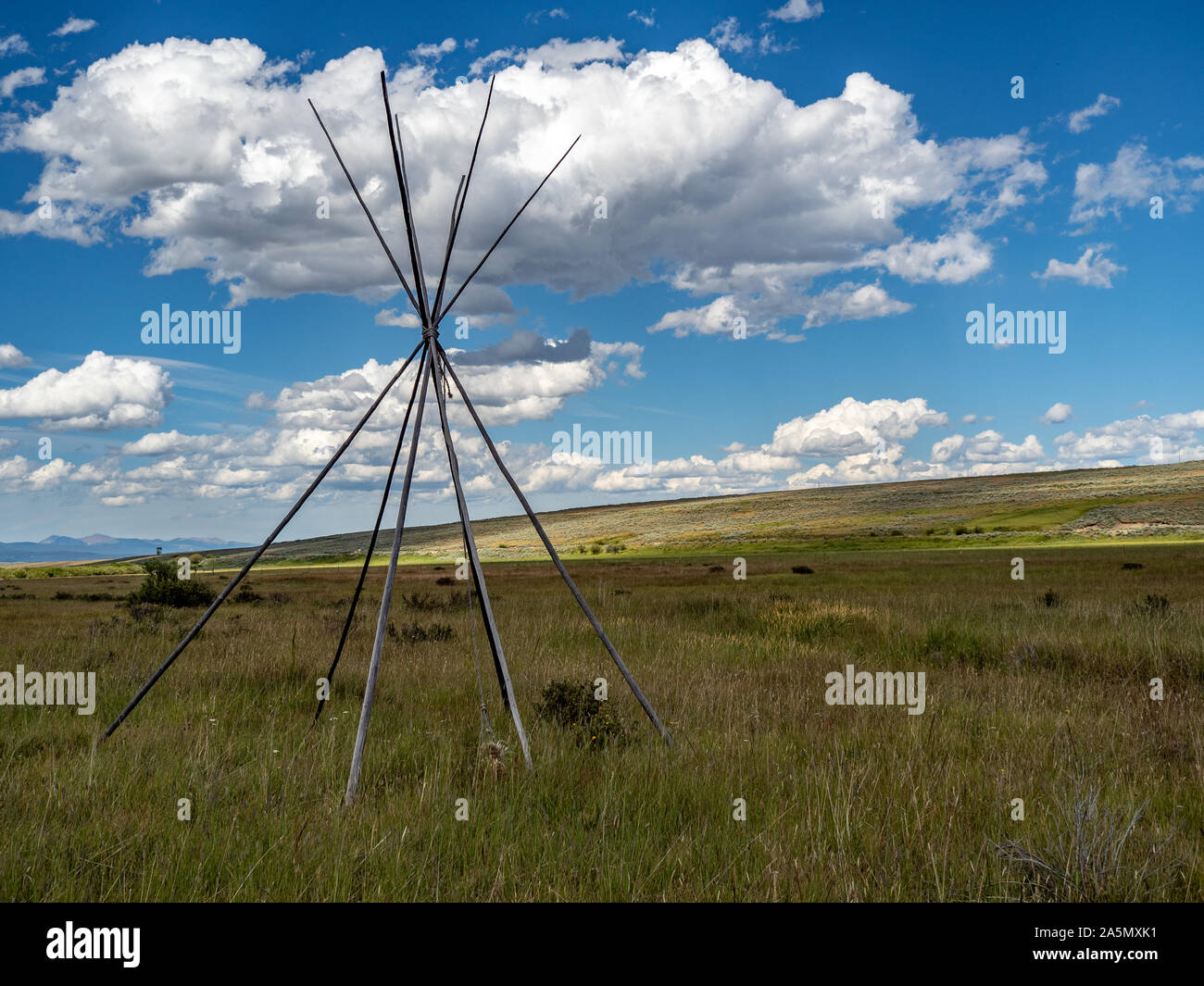 Teepee frames with blue sky and billowing white clouds in background ...