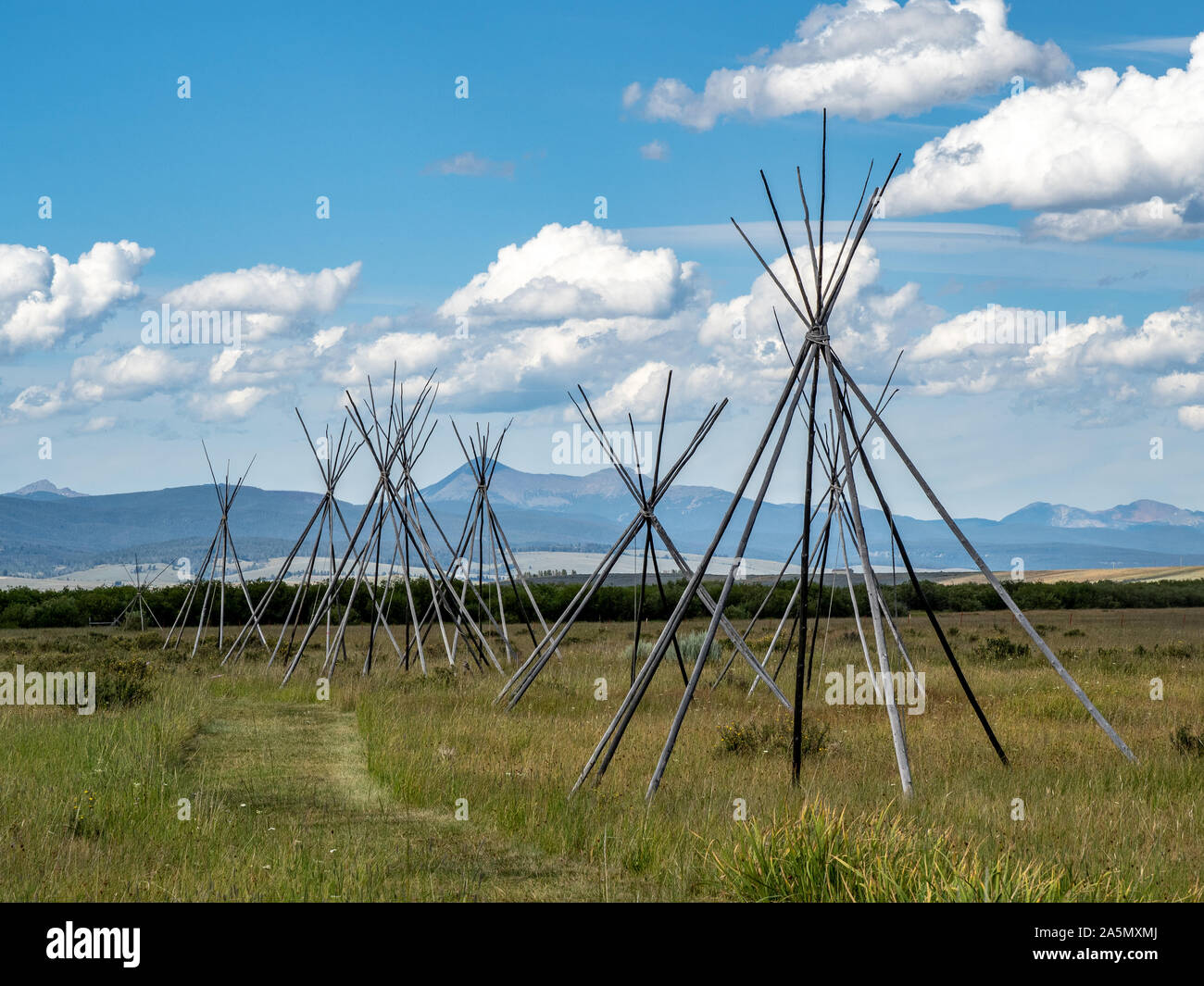 Teepee frames with blue sky and billowing white clouds in background ...