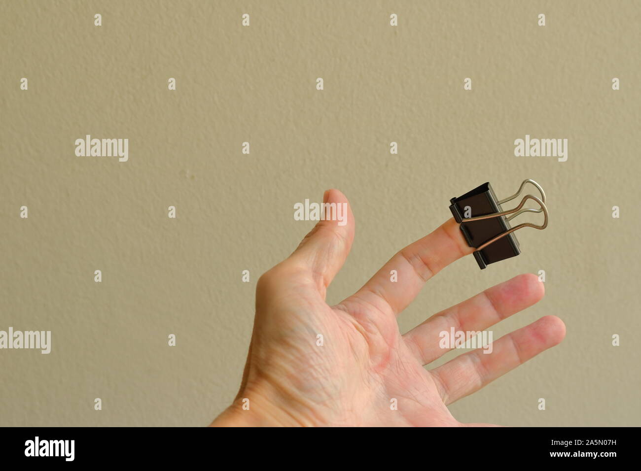 Closeup left index finger pinched by binder clip over light wall ...