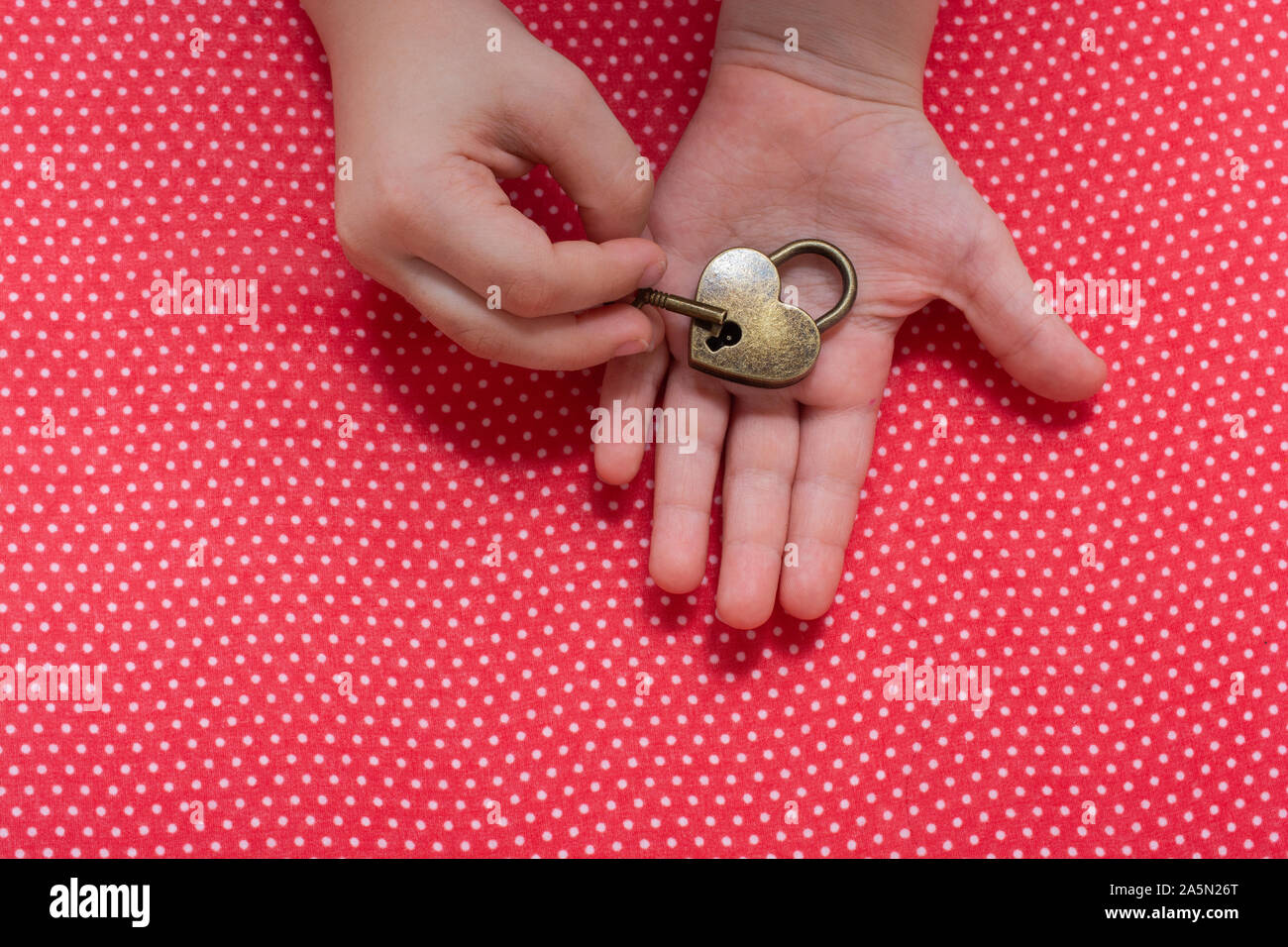 Hand holding a heart shaped lock and key on a red background Stock ...