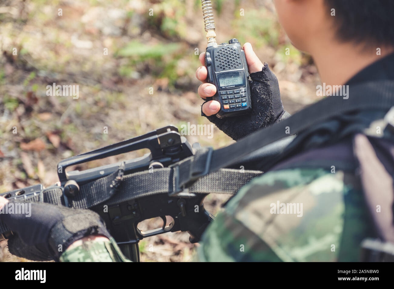 Closeup image of an armed soldier holding and using radio communication ...
