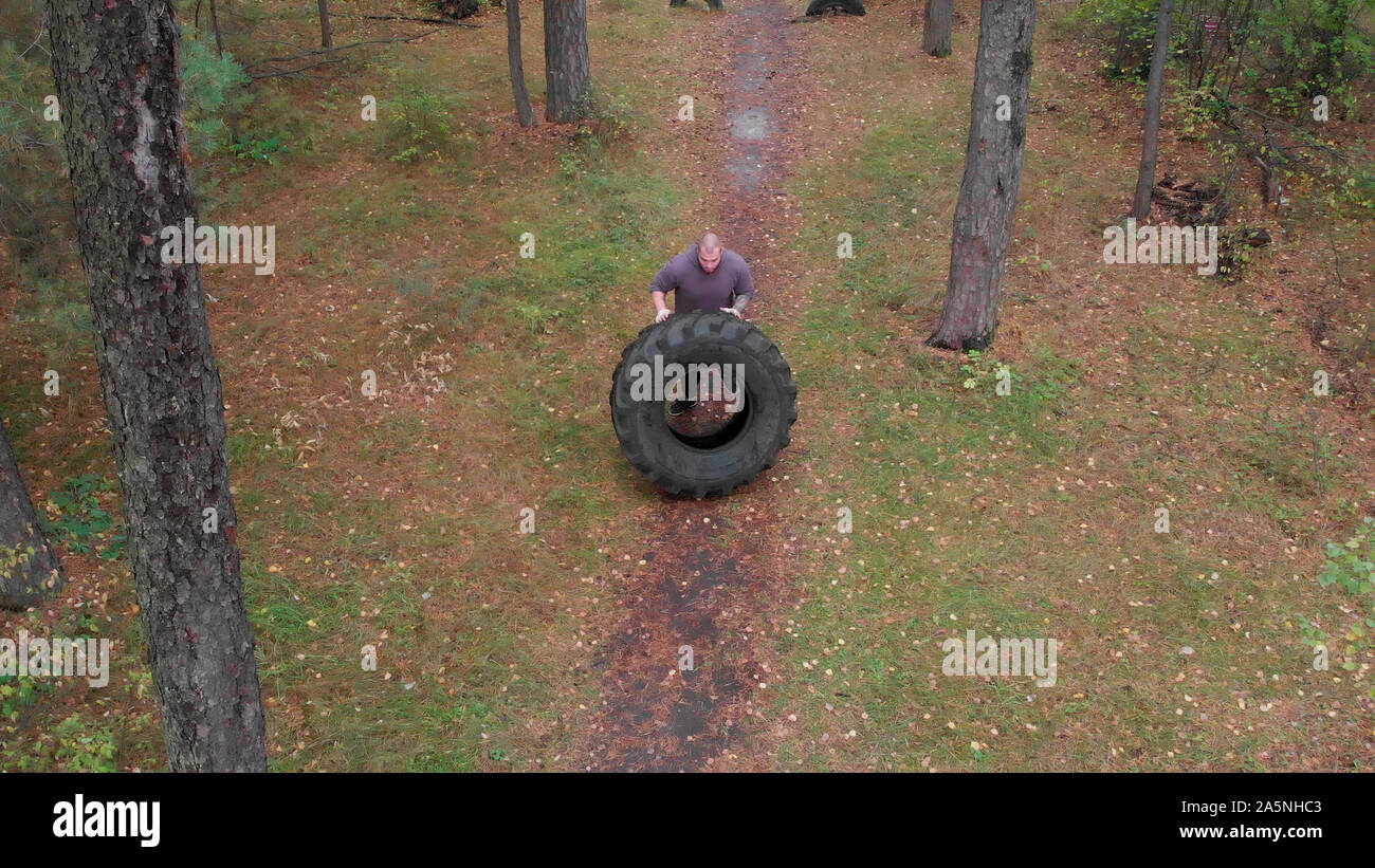 A tough man bodybuilder pushes over the tire on the ground in the ...