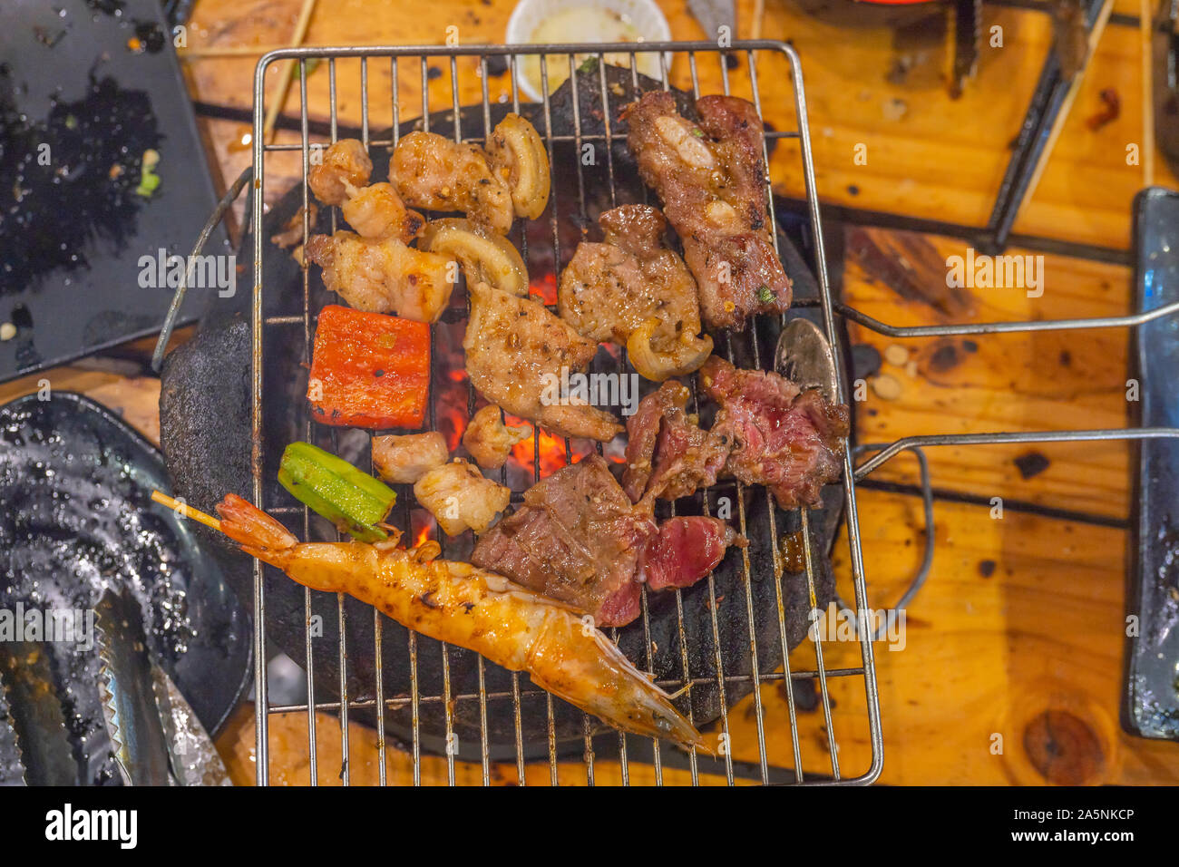 Grilling marinated meats and shrimp on flaming charcoal stove Stock ...