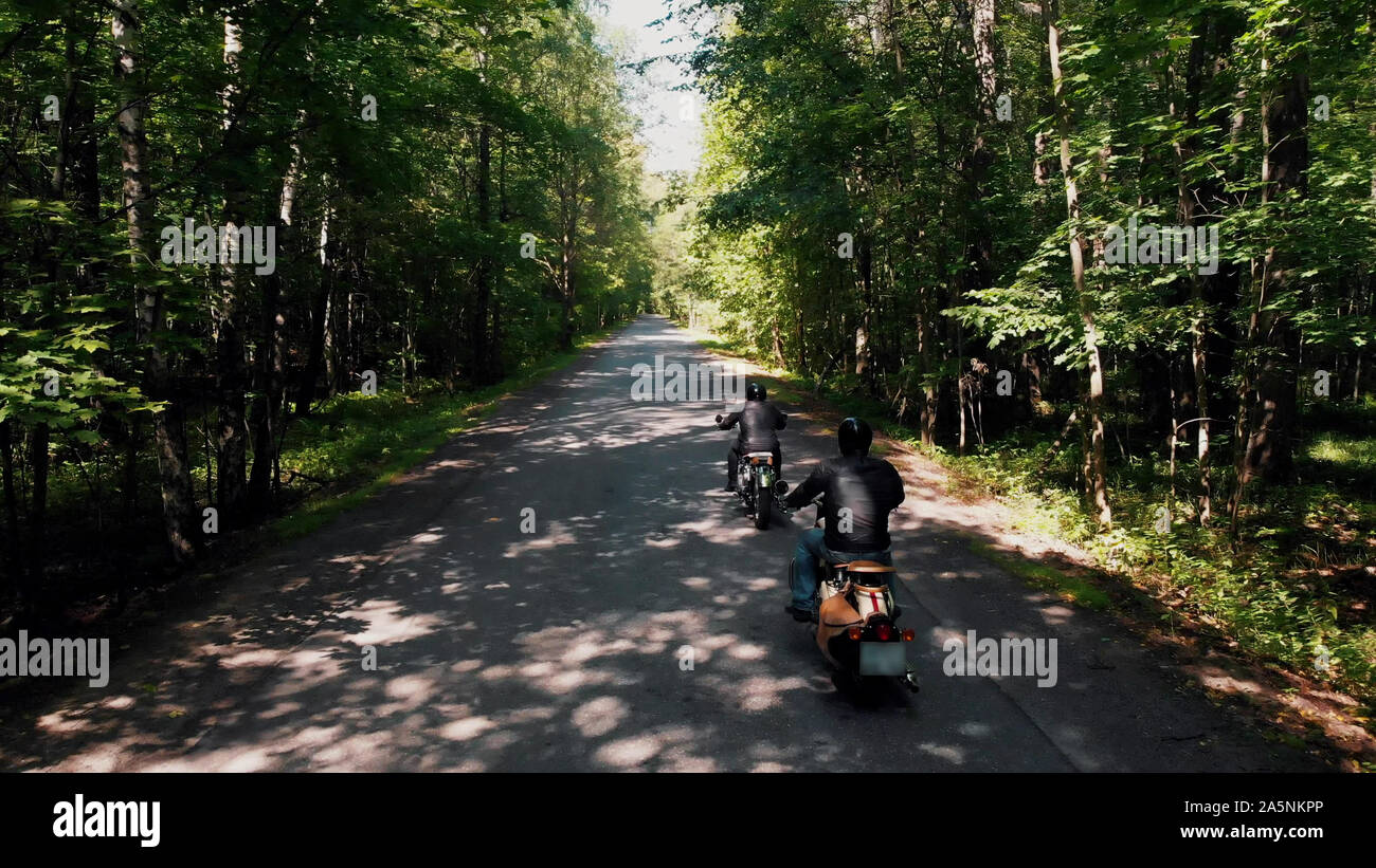 Bikers are riding by each other along the road in the green forest ...