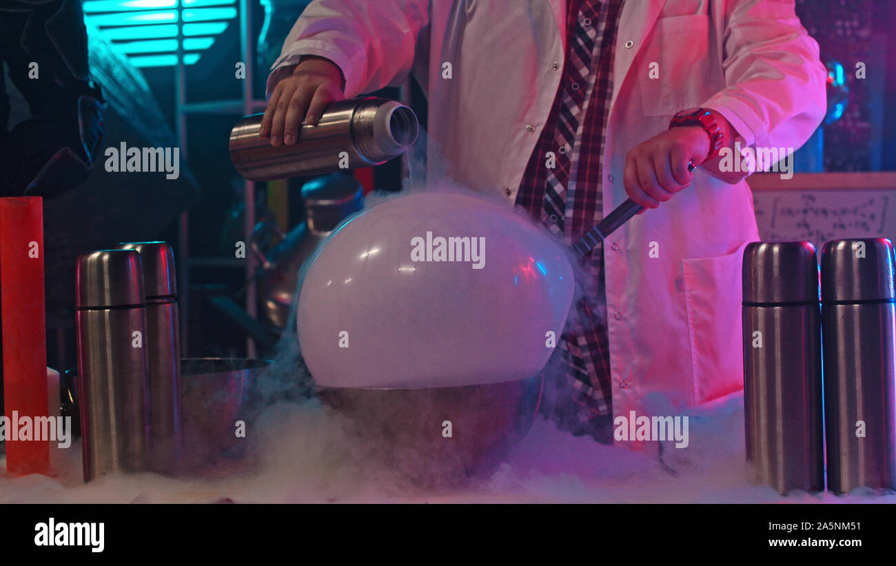 A man is pouring liquid nitrogen from a thermos on a ballon - indoors ...