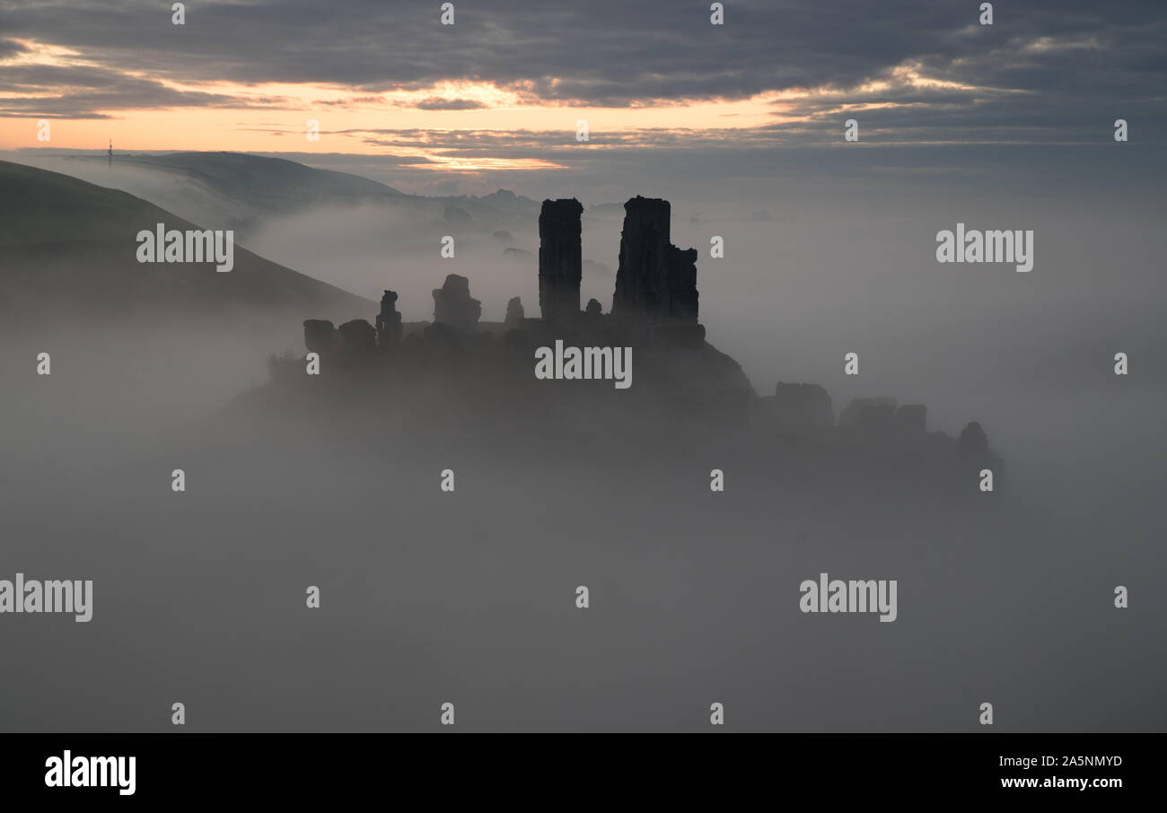 The sun begins to rise behind a mist covered Corfe Castle in Dorset ...