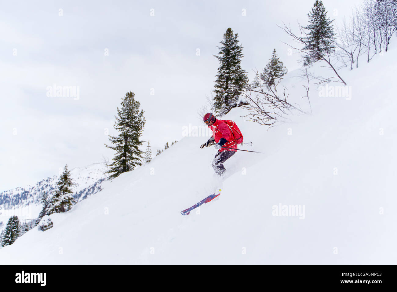 Side photo of sports man in red jacket and with backpack skiing in ...