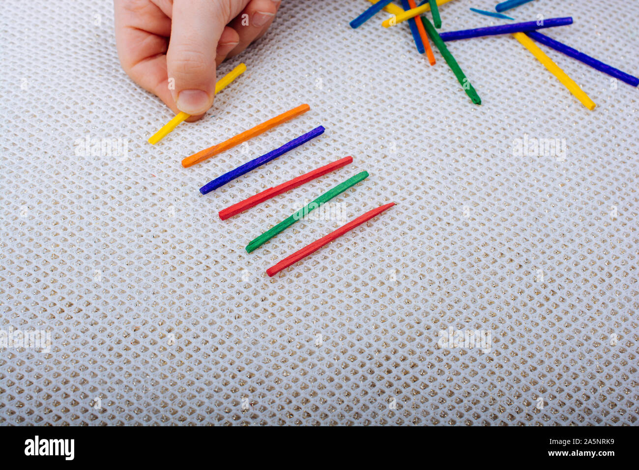 Kid playing with coloured wooden sticks for creativity on white ...