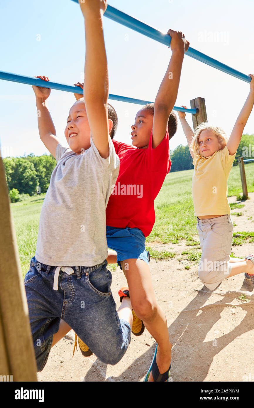 Three multicultural boys are shimmying and doing gymnastics on a jungle ...